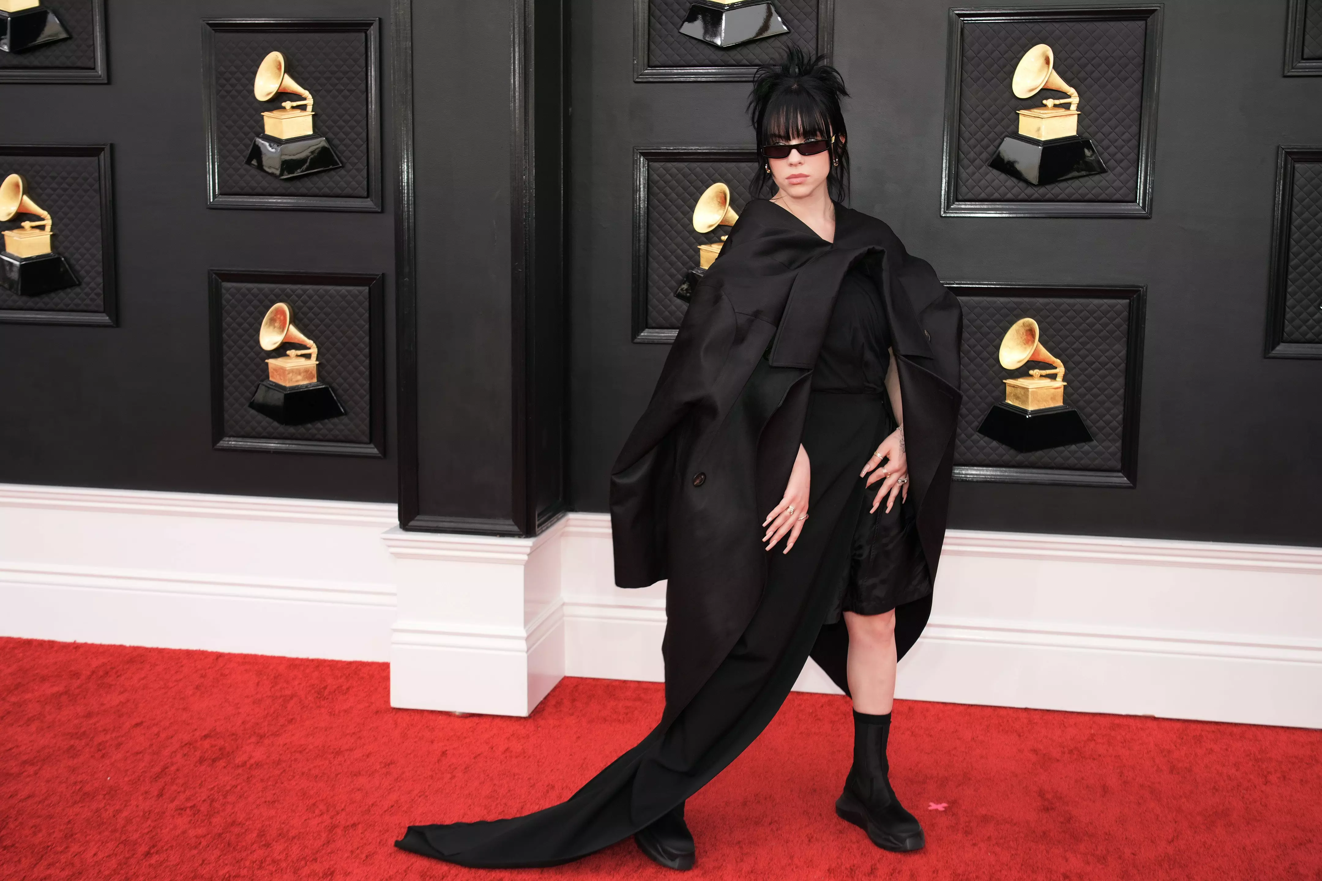 Billie Eilish usa um vestido preto assimétrico com sapatos flatform no tapete vermelho do Grammy 2022.