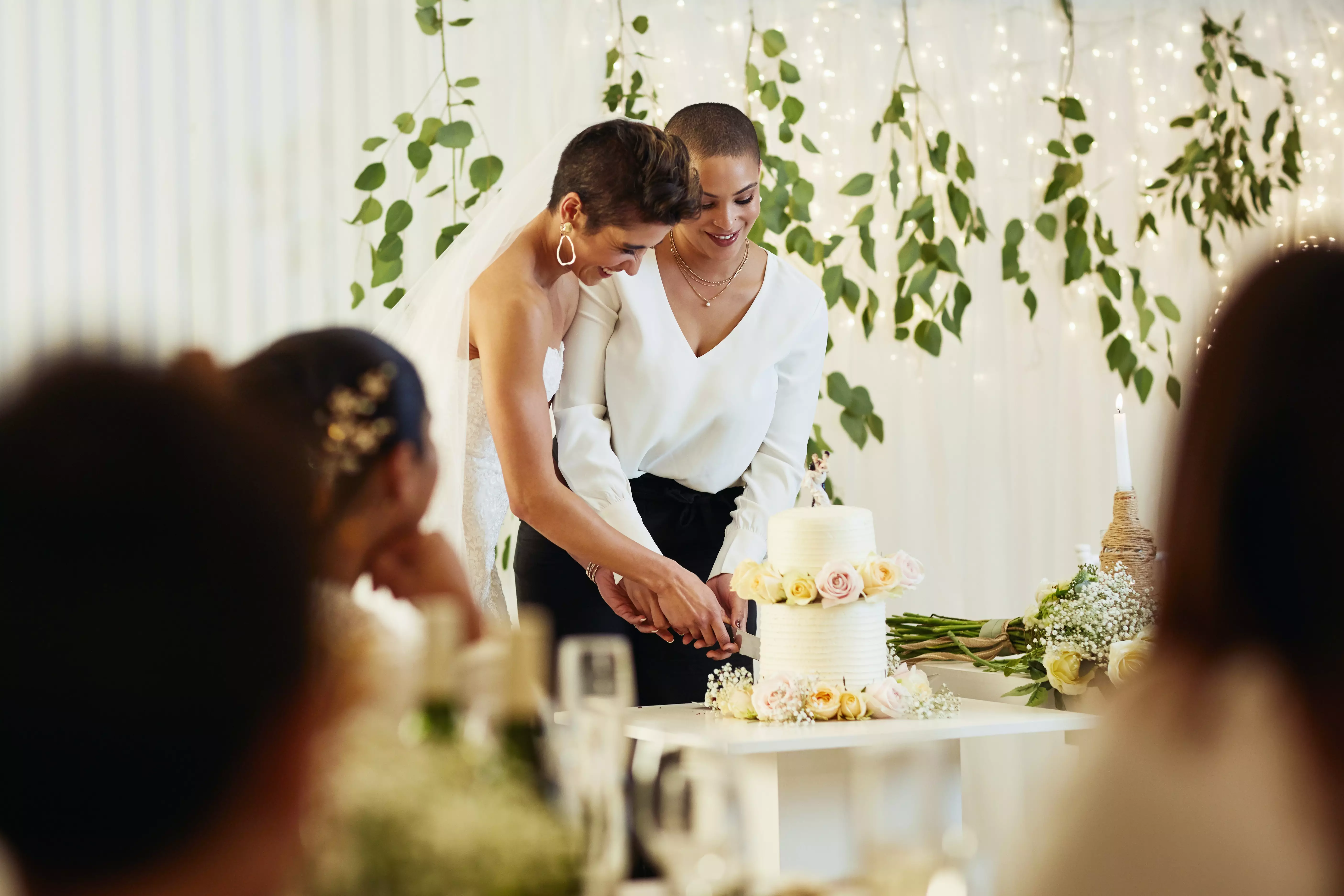 Una pareja cortando su pastel en su boda, con algunos invitados preguntándose cuánto cuesta asistir...