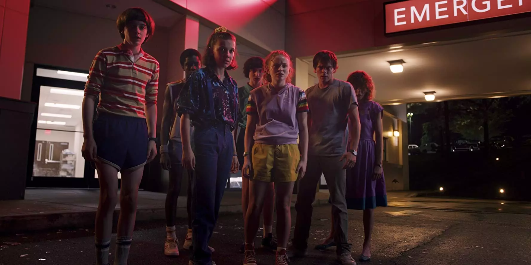 De Besetzung vun 'Stranger Things' steet ausserhalb vun der Starcourt Mall an enger grujeleger Szen.