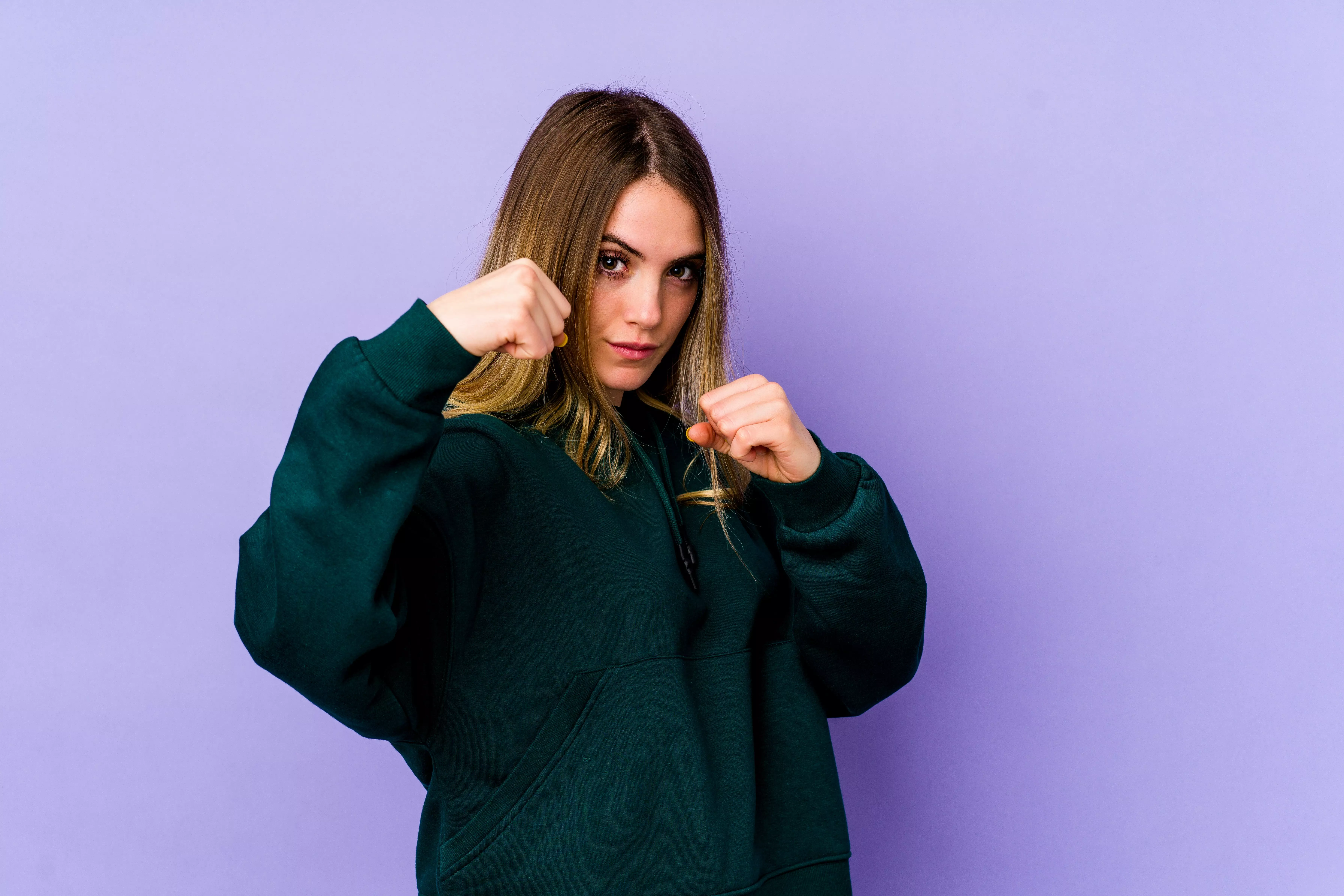 Jeune femme caucasienne isolée sur fond violet lançant un coup de poing, colère, combat à cause d'une dispute...