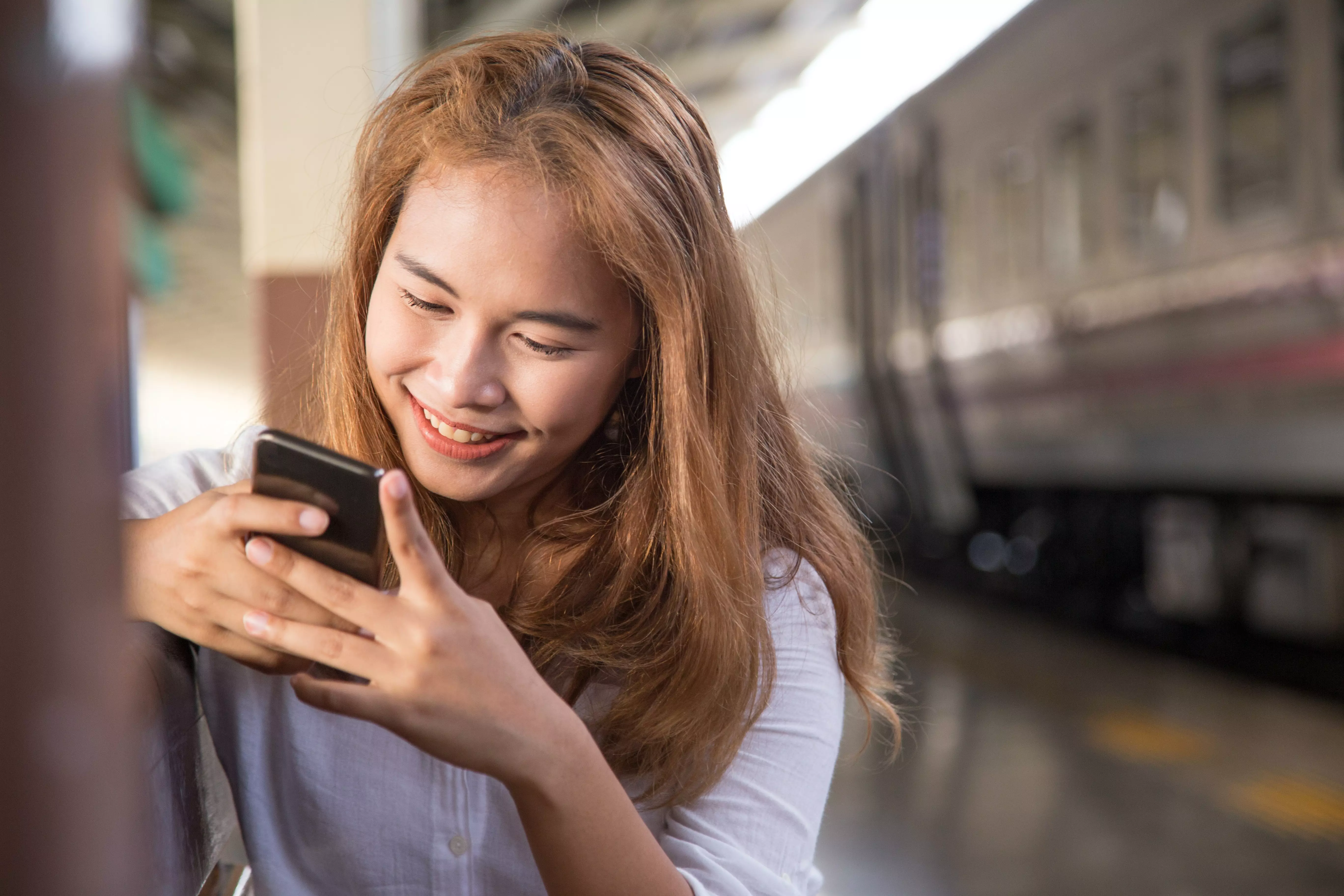 Ung kvinne chatter eller sender meldinger mens hun bruker mobiltelefonen eller smarttelefonen under reise...