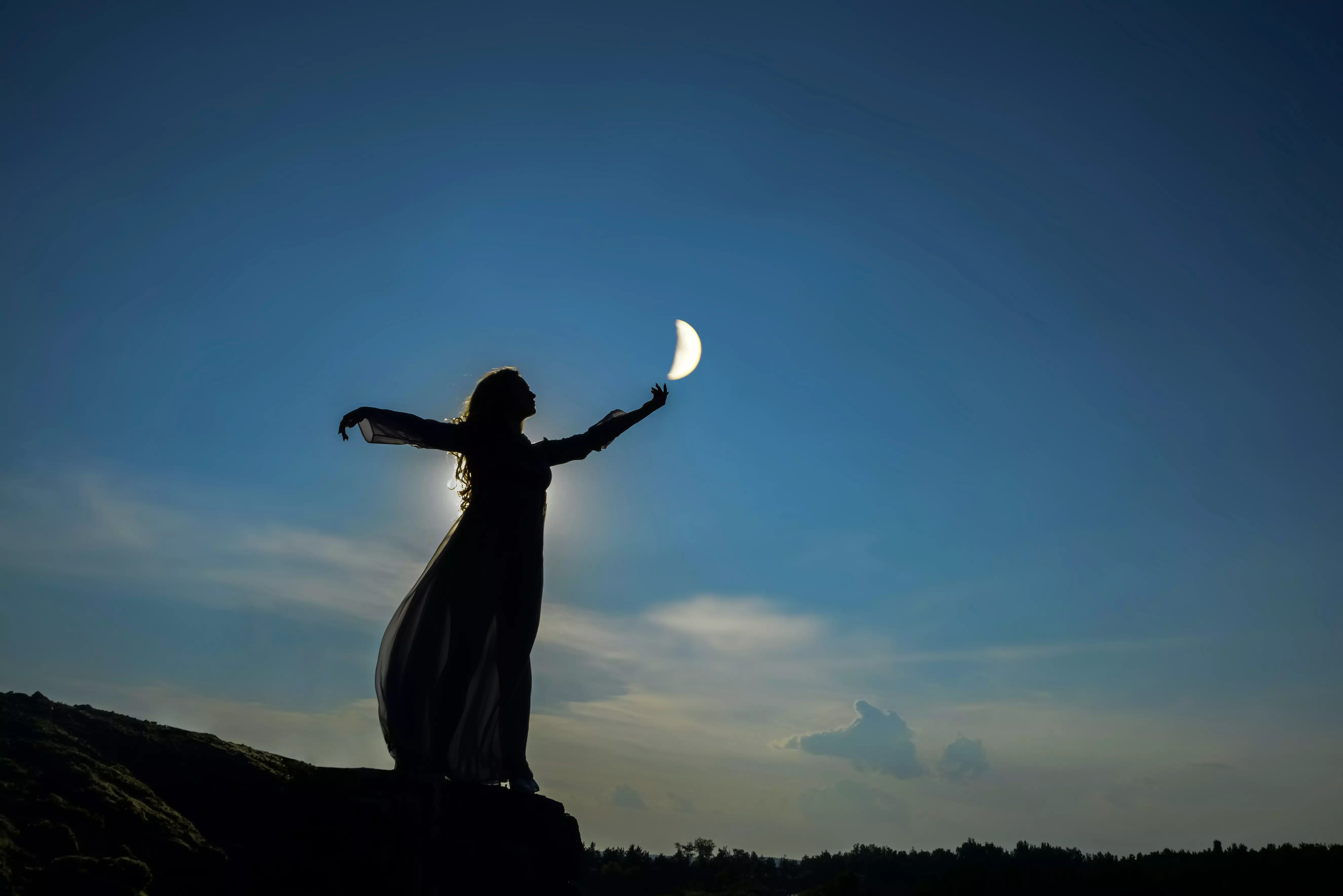 silhoutee de femme debout au sommet de la montagne. une femme tient dans la main une lune qui pousse au-dessus d'un arbre forestier...