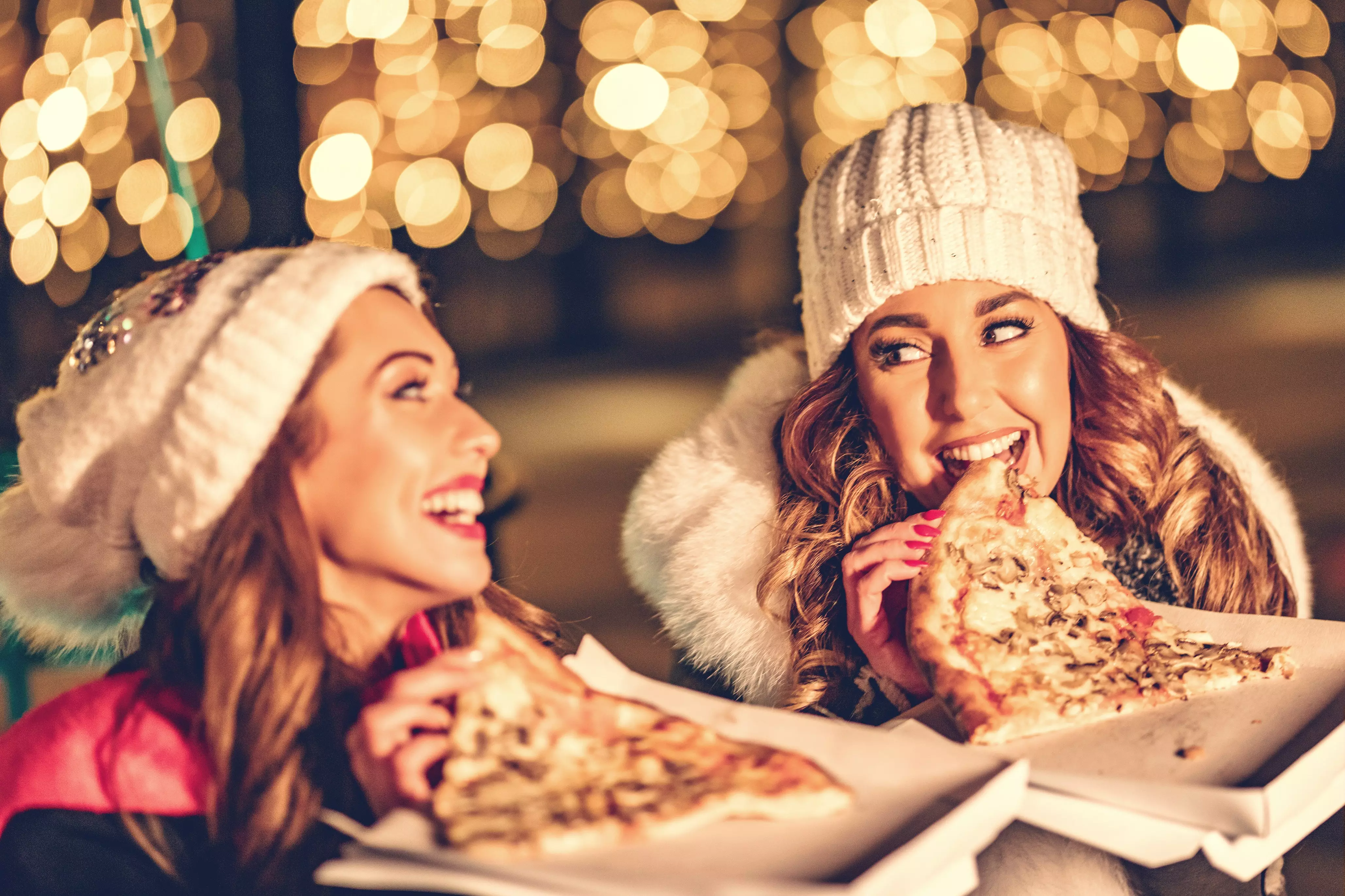 Dvě ženy si venku užívají rande a smějí se s plátky pizzy v rukou.