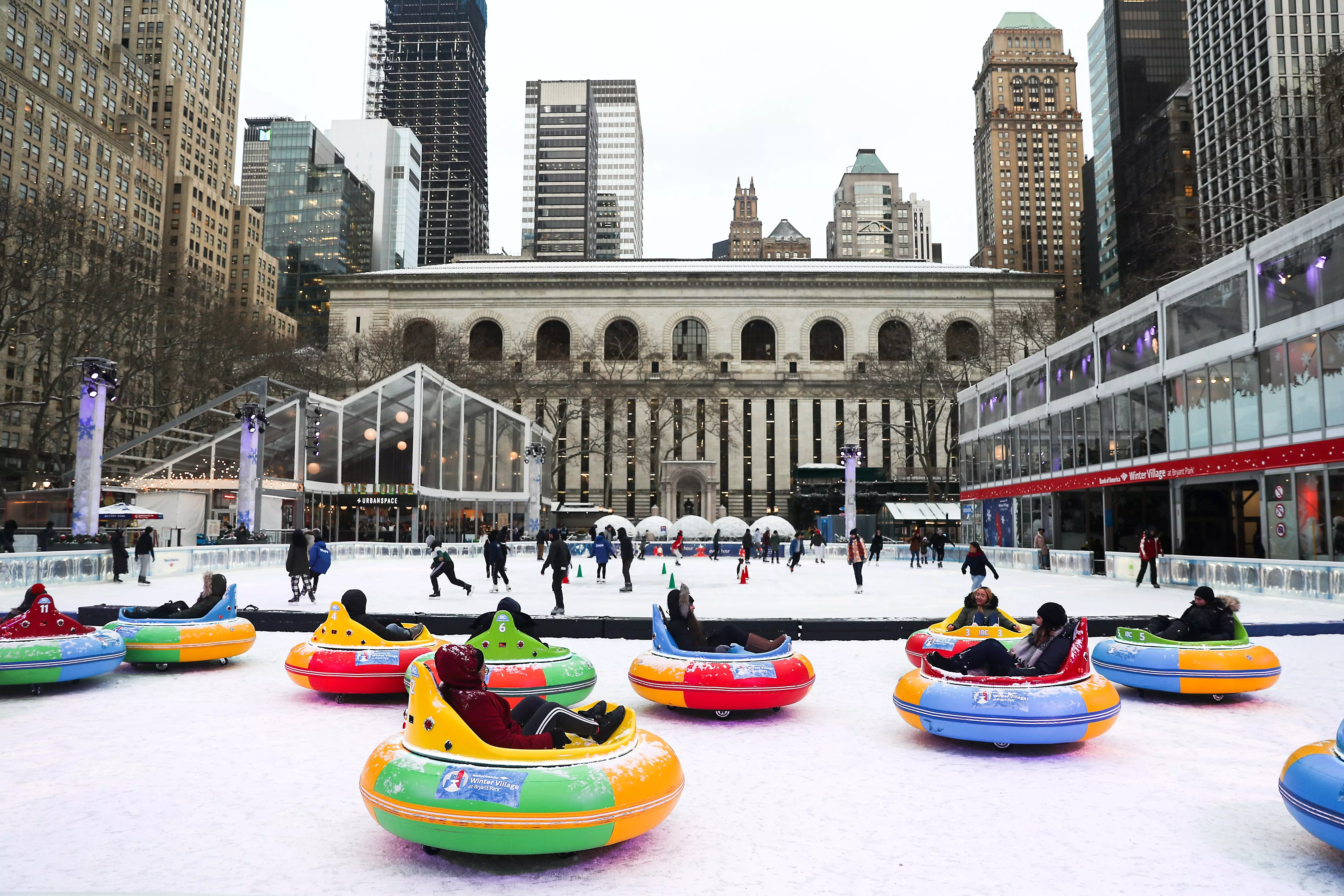 Călătorii se plimbă cu mașini cu bară de protecție pe gheață în timpul FrostFest din Bryant Park din New York City.