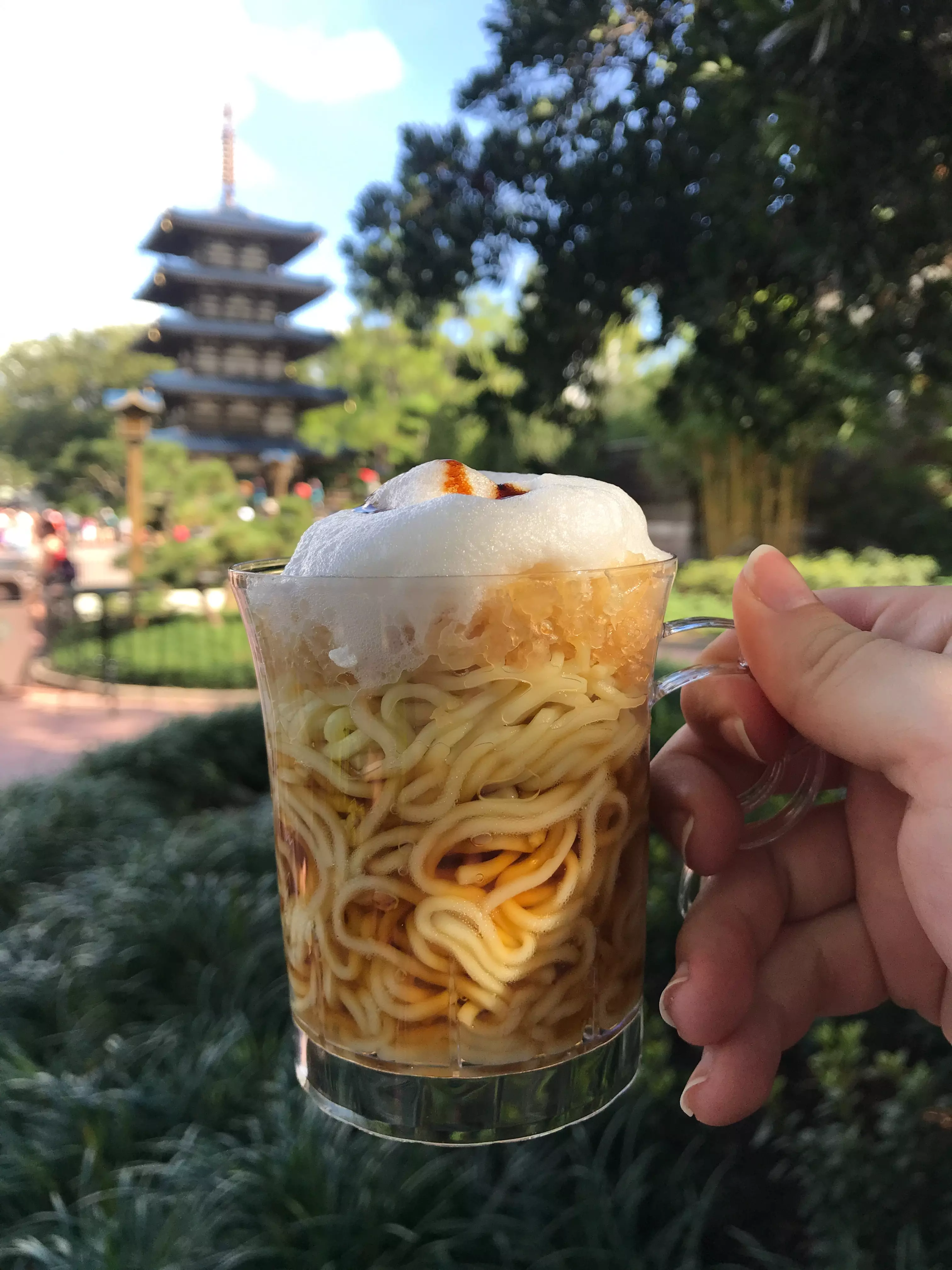 En kvindes hånd holder en kop afkølet ramen op med skum på toppen på Disneys Food & Wine Festival på...