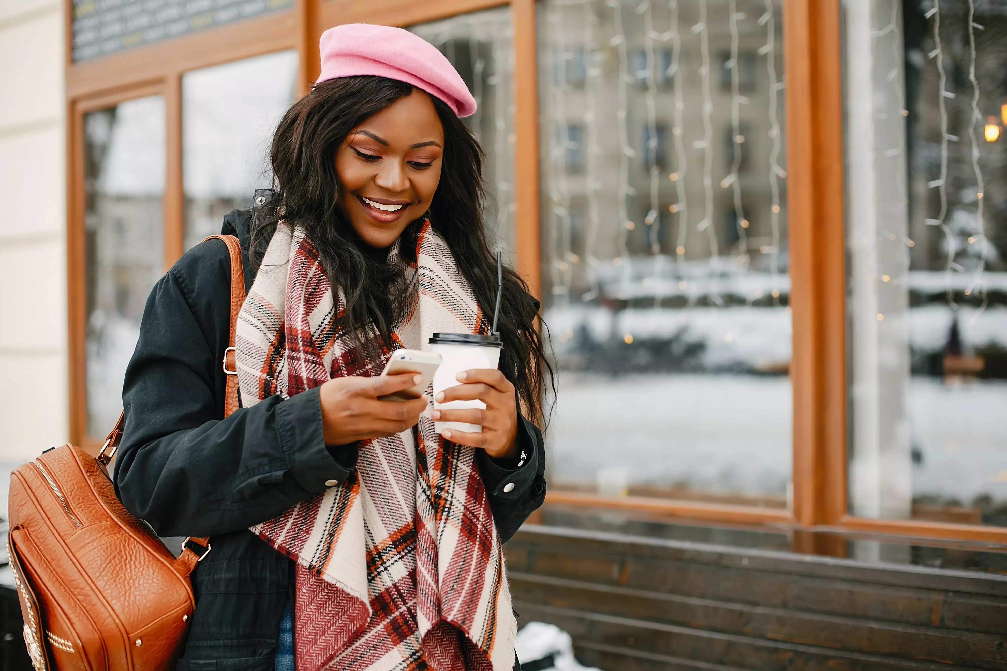 En fashionabel kvinna går runt i en stad med en ryggsäck, halsduk och rosa hatt och tittar på sin telefon...